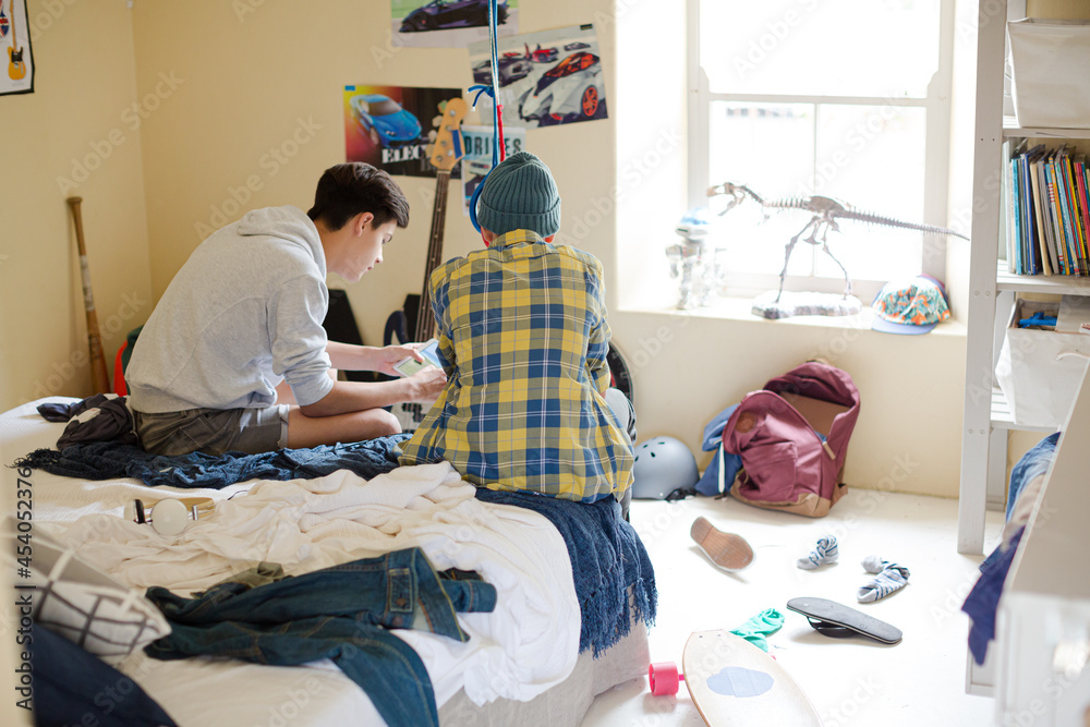 Two teenage boys sitting on bed in messy room Stock Photo | Adobe Stock