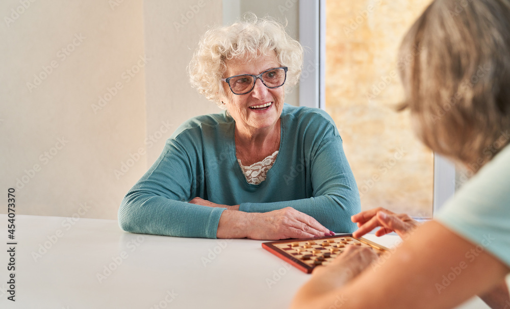Happy elderly woman plays checkers with a friend Stock Photo | Adobe Stock