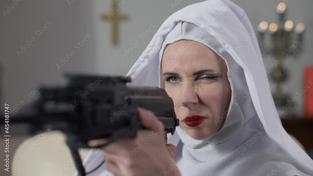 Close-up of serious woman in nun costume aiming with gun indoors ...