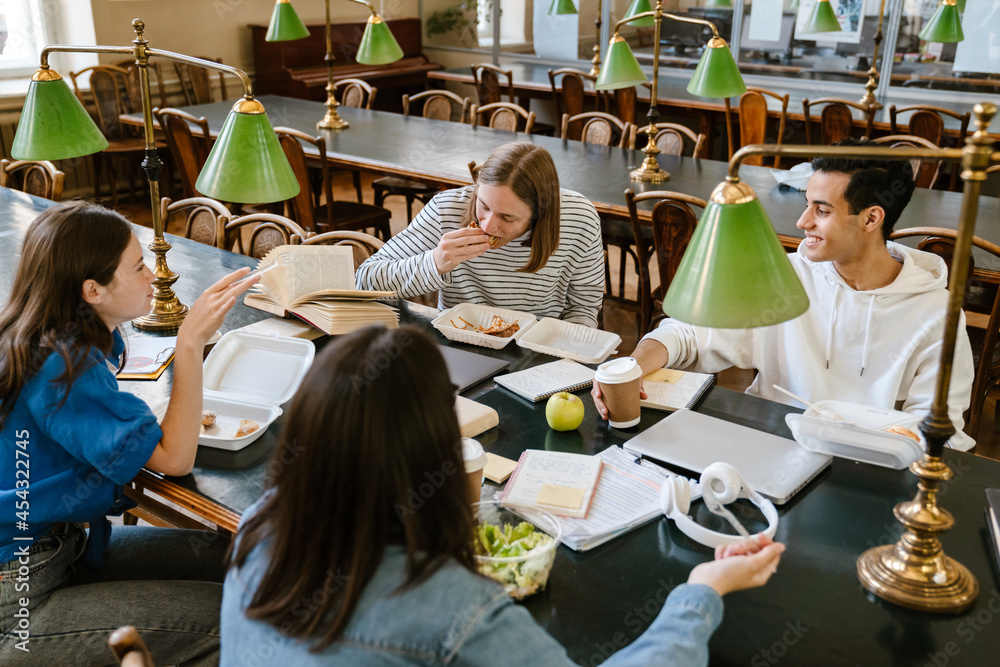 Young multiracial students talking while having lunch at library Stock ...