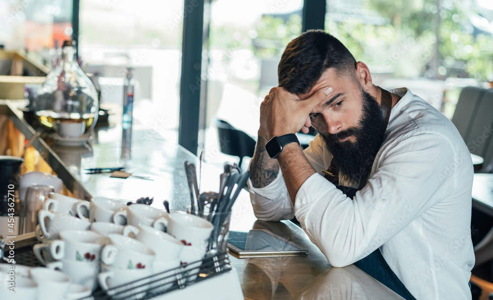 Worried Barista Using Digital Tablet in a Cafe. Distraught sad waiter ...