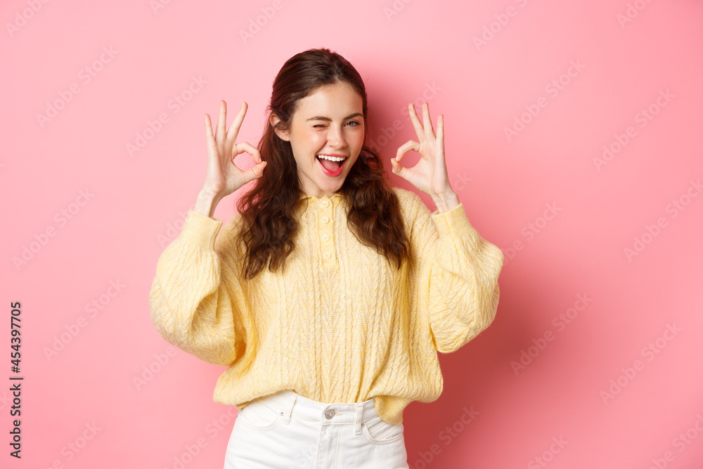 Portrait of cheerful pretty girl winking and saying yes, showing okay ...