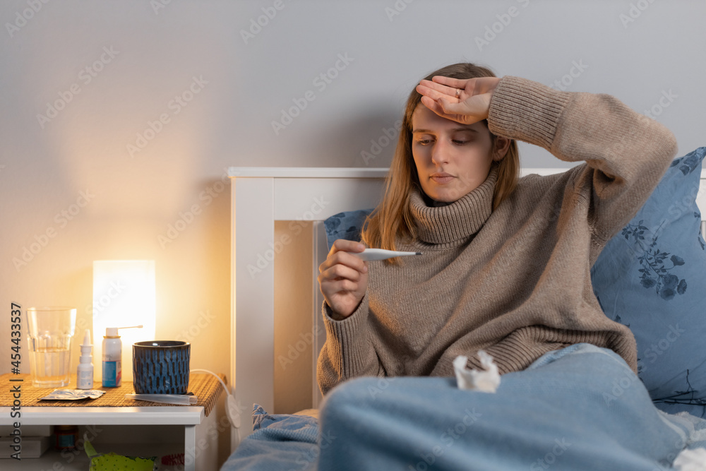 Attractive young woman in beige sweater sitting in bed, touching head ...