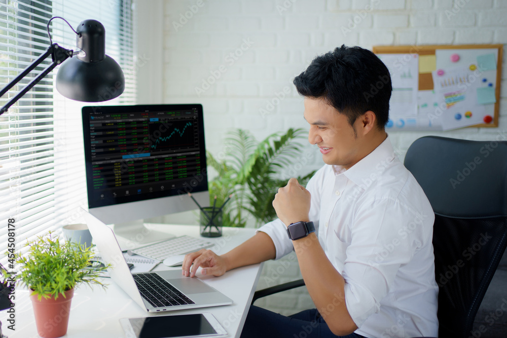 Young trader working with laptop while sitting in his modern office. He ...