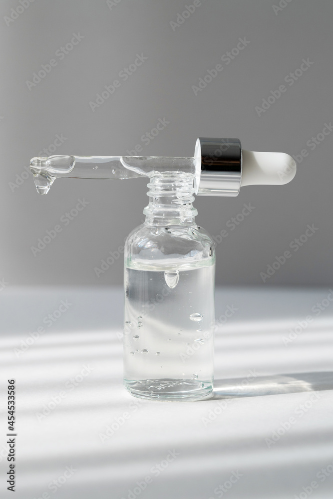 Opened facial serum in transparent bottle and dropper with drop on grey ...