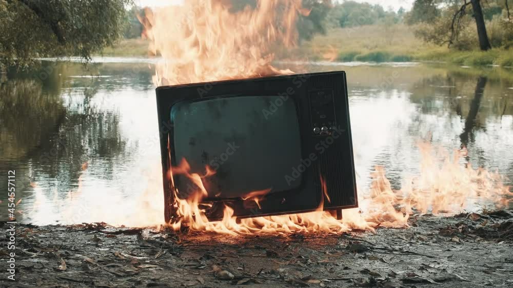 Retro vintage TV flares up and burns with fire next to the river ...