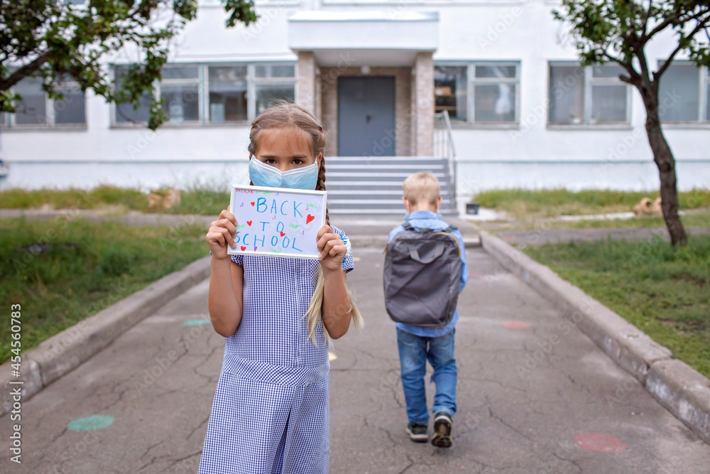 Foto de Elementary school girl in medical mask holds picture with back ...