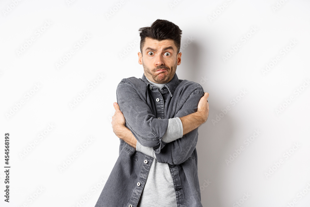 Funny young man hugging himself and grimacing, feeling embarrassed and ...