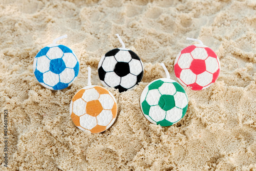Five multi-colored soccer balls on white sand as a symbol of the ...