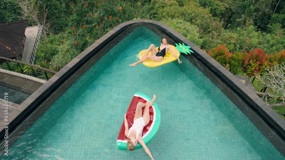two women floating in swimming pool lying on inflatables best friends ...