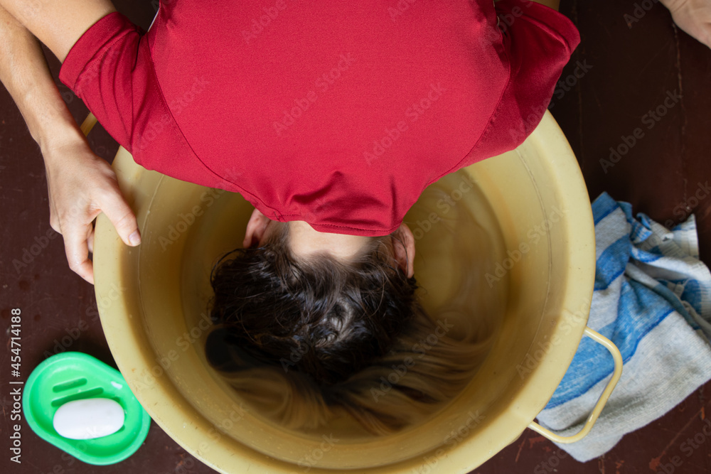 Foto de young girl washes her hair in a plastic bowl on the floor of ...