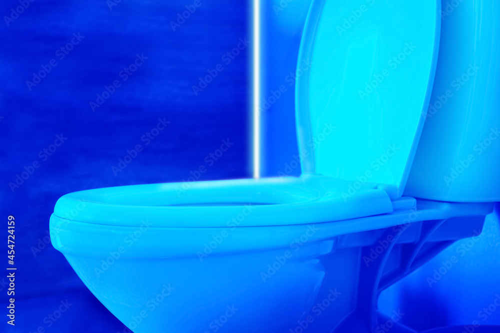 Toilet bowl in public restroom lit with UV blue light, closeup view ...