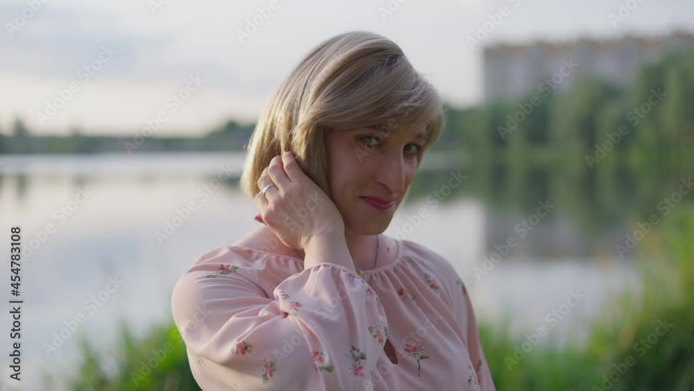 Portrait of shy Caucasian transgender woman posing outdoors at sunset ...