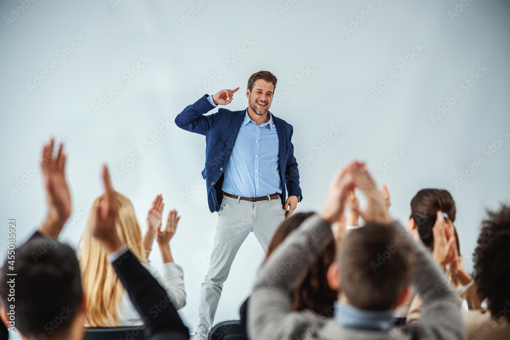 Smiling motivational speaker standing in front of his audience who is ...