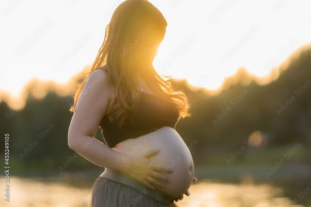 Rays of sunset illuminating a pregnant woman as she touches her belly ...
