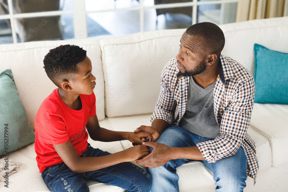 Serious african american father and son sitting on couch in living room ...