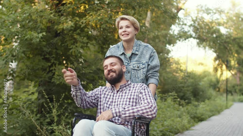 Woman rolls emotional disabled man in wheelchair, who points way with ...