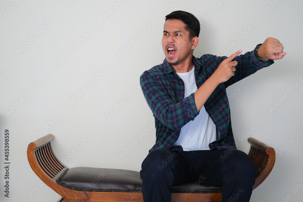 Adult Asian man sitting in a chair and showing angry face expression ...
