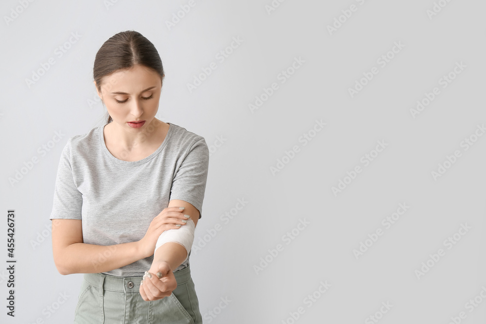 Young woman with bandaged arm on light background Stock Photo | Adobe Stock