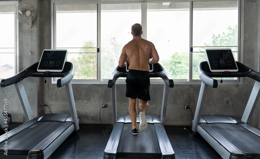 Back view of man running on treadmill in the gym. Sportive people ...
