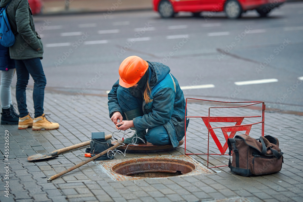 Utility worker sits in front of an open sewer hatch on city street ...