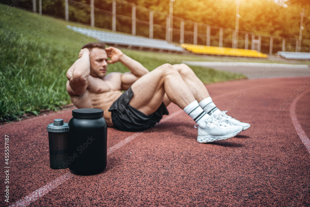 protein whey drink in black container and muscular athlete exercising ...