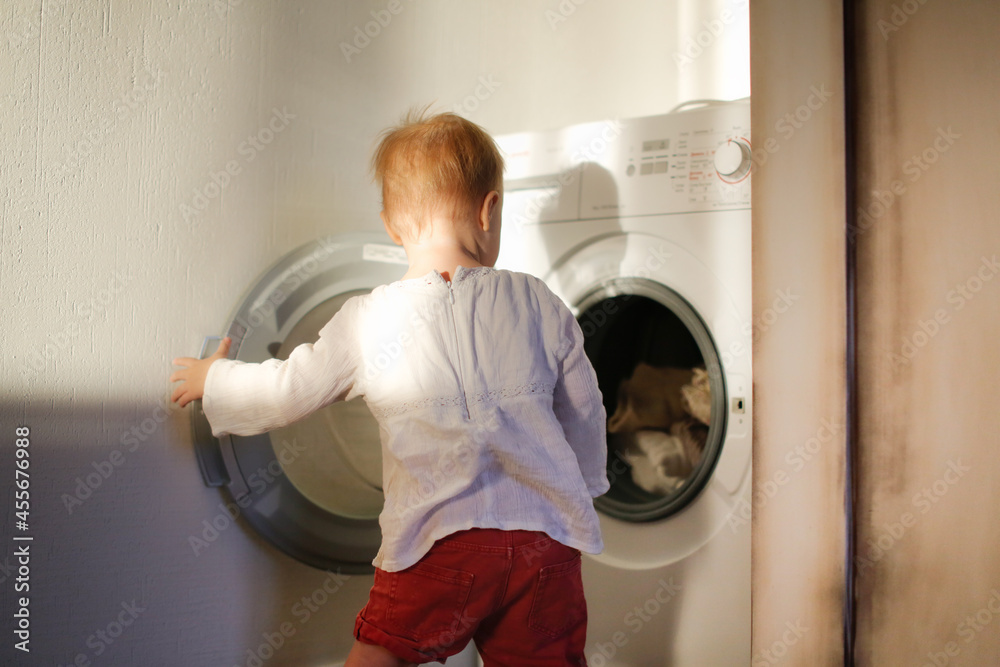 Toddler child with washing machine, soft focus and evening light. The ...