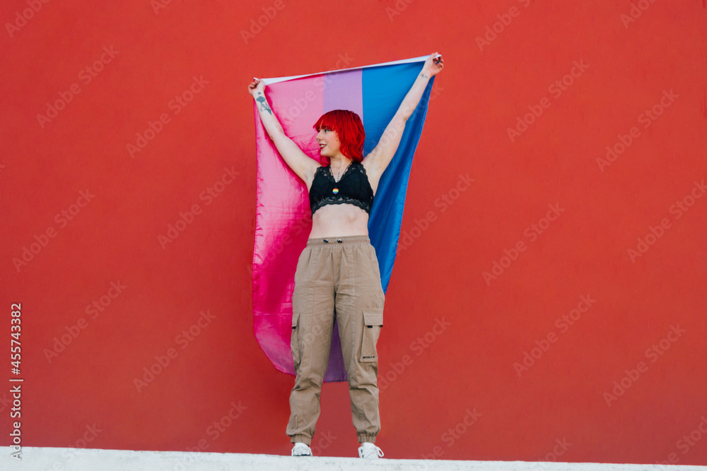 Young woman waving bisexual pride flag standing against red background ...