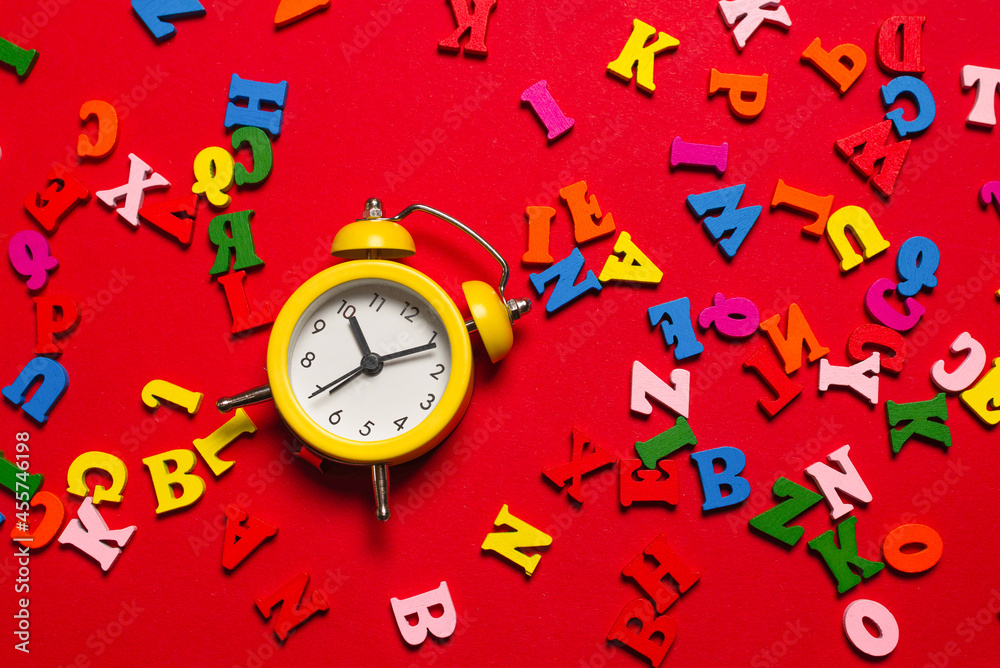 Random colorful alphabet and yellow alarm clock on a red background ...