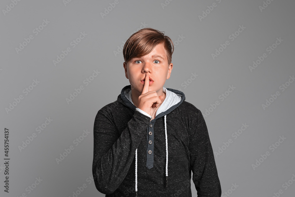 Serious young boy standing on gray studio background, looking at camera ...