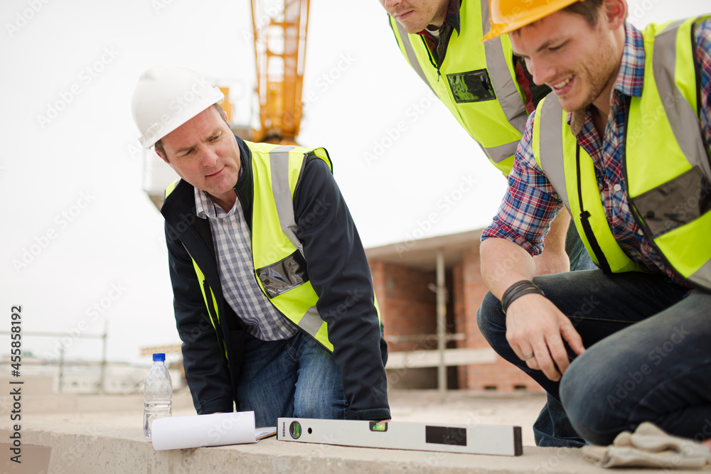 Construction workers using level tool below crane at construction site ...