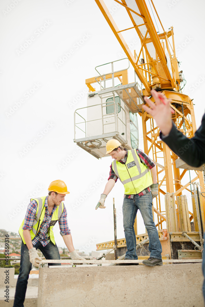 Construction workers using level tool below crane at construction site ...