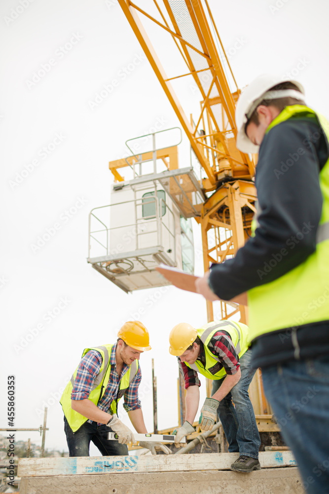 Construction workers using level tool below crane at construction site ...