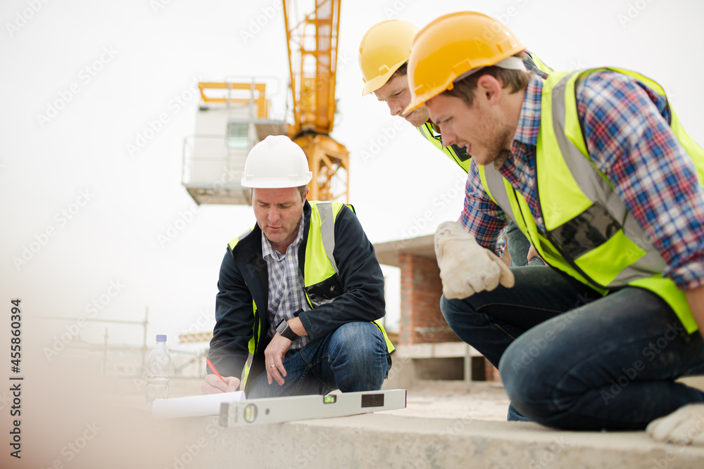 Construction workers using level tool below crane at construction site ...