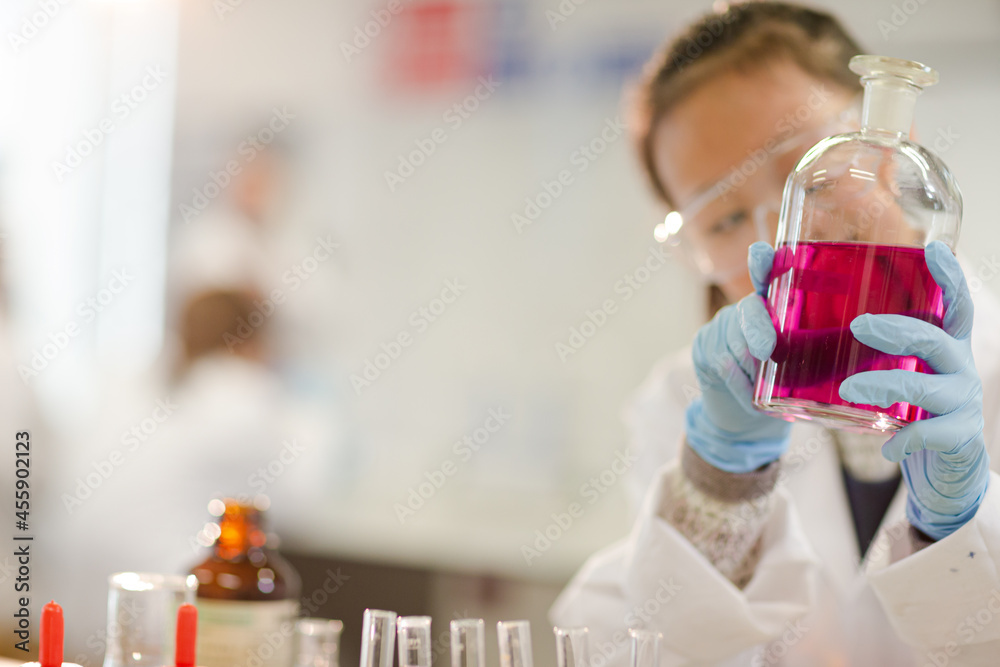 Girl student examining pink liquid, conducting scientific experiment in ...
