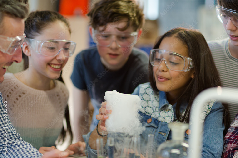 Male teacher and students watching chemical reaction, conducting ...
