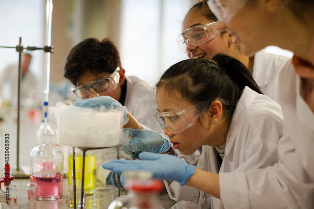 Female teacher and students watching scientific experiment chemical ...