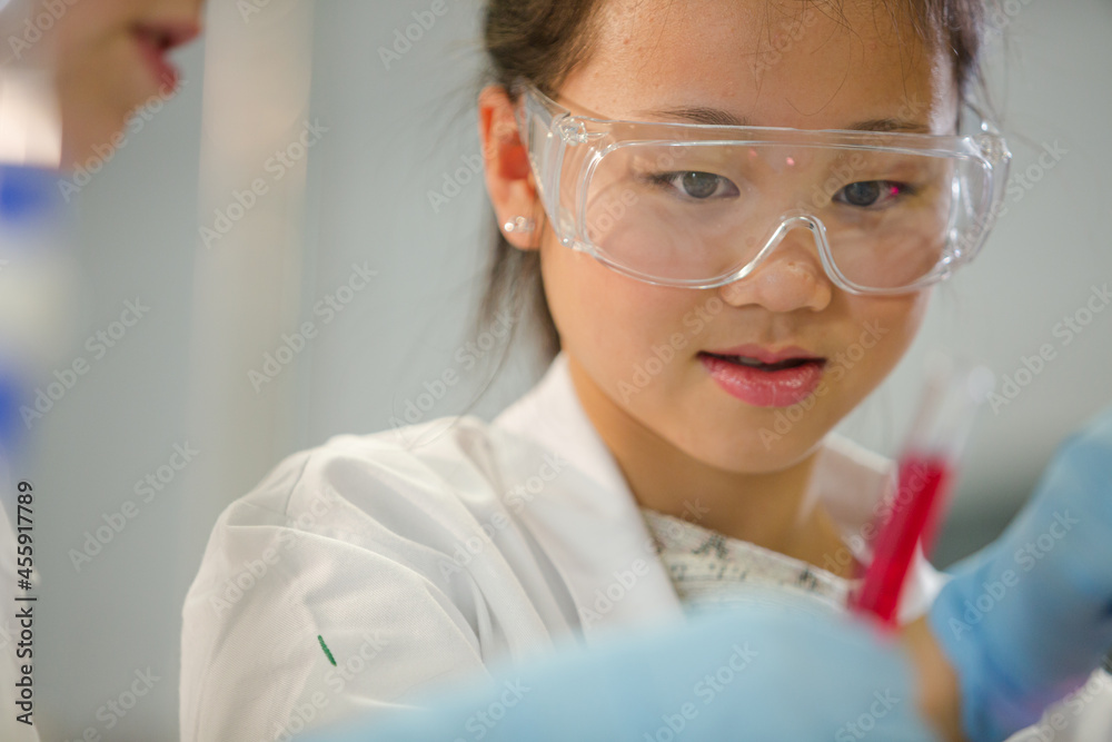 Girl student examining pink liquid, conducting scientific experiment in ...