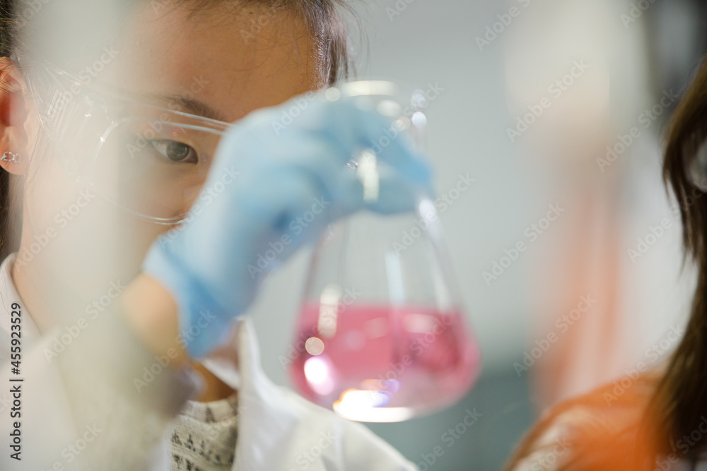 Girl student examining pink liquid, conducting scientific experiment in ...