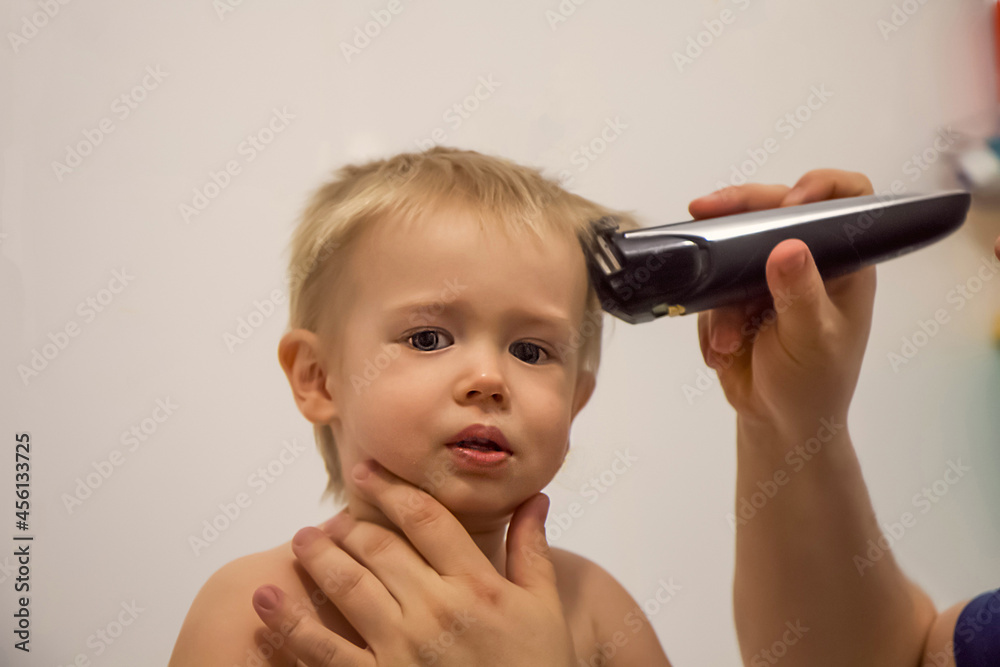Kid boy with blond hairs getting his first haircut with razor blade in ...