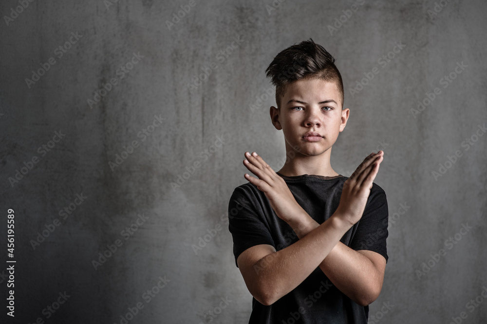 Sad boy teenager standing on a dark background crossed his arms on his ...