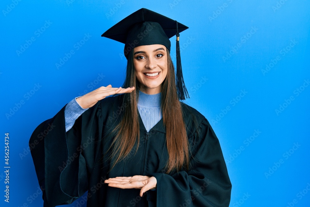 Beautiful brunette young woman wearing graduation cap and ceremony robe ...