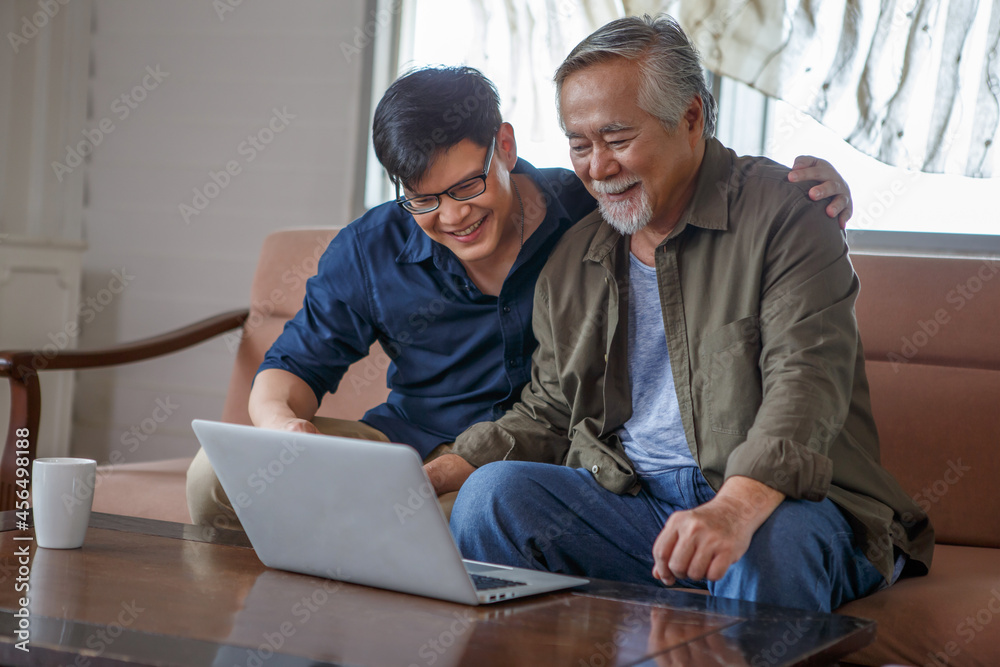 happy asian adult son and senior father sitting on sofa using laptop ...