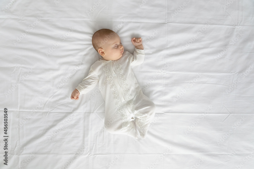 Peaceful adorable baby in bodysuit sleeping on double bed with white ...