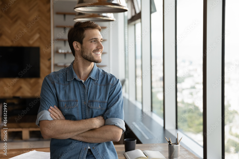 Smiling male employee stand at workplace look in window distance ...