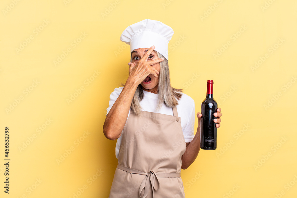middle age chef woman looking shocked, scared or terrified, covering ...