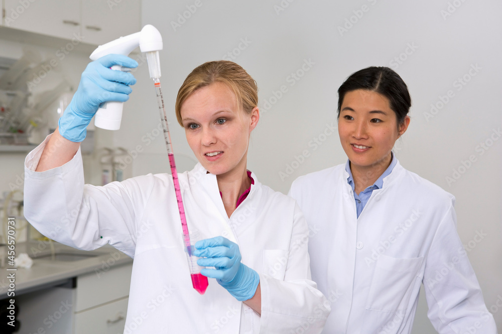 Female scientists at work in laboratory, pipetting liquid for reaction ...