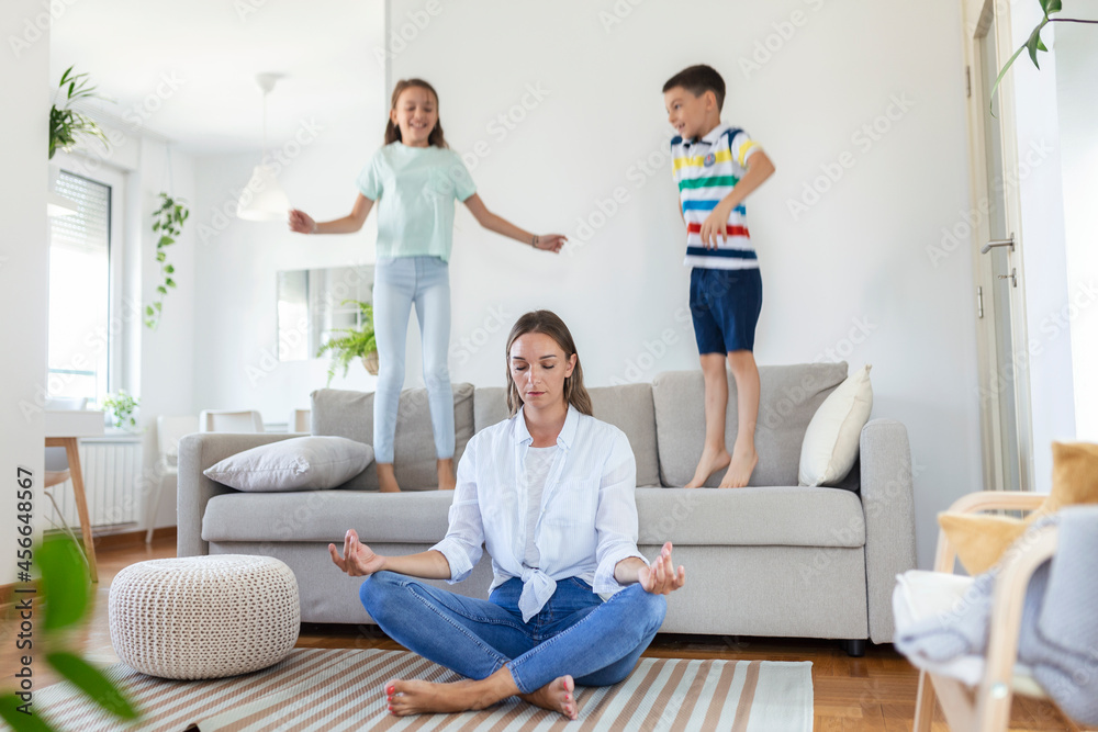 Young mother with closed eyes meditating in lotus pose on floor trying ...