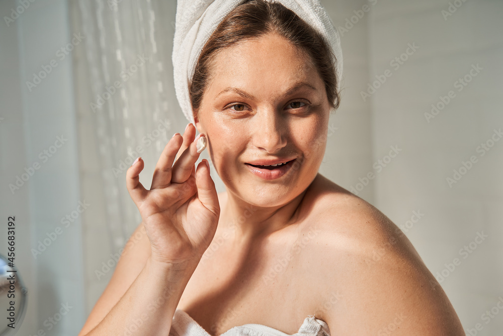 Woman taking body lotion into her finger and looking at the camera with ...