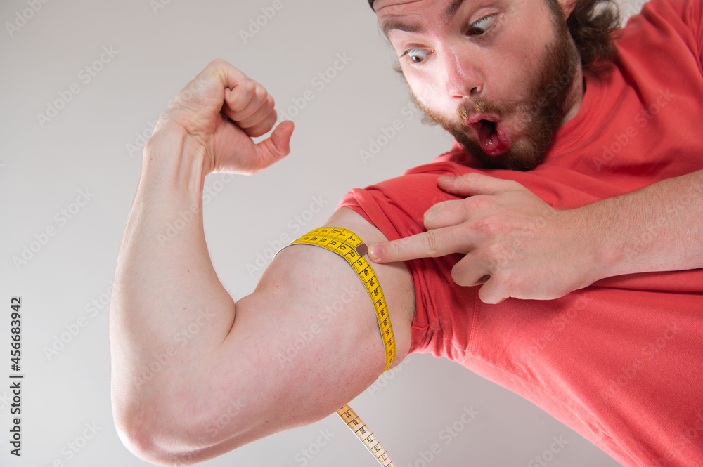 Bearded funny man measuring biceps, muscles of his arm with a yellow ...